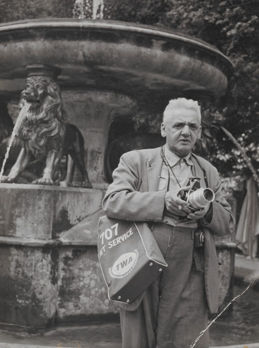 Weegee with Camera and TWA Bag in Front of Fountain